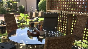 Um pátio externo com mesa de vidro redonda, cadeiras de vime e cerca de madeira.