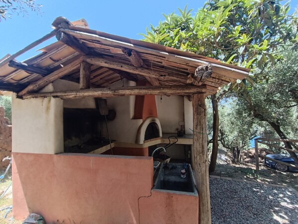 Uma cozinha rústica ao ar livre, com telhado de madeira, pia e fogão.