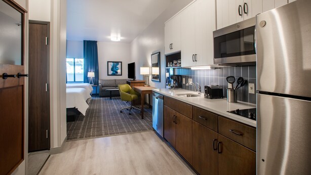 Quarto de hotel moderno com cozinha compacta, cama, escrivaninha e cadeira.