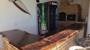 Uma área de bar com balcão de tijolos, refrigerador Heineken e lareira de tijolos.