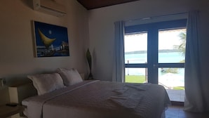 Quarto com cama grande, um quadro na parede e vista para o mar pela janela.