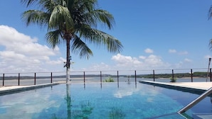 Uma piscina cristalina com uma palmeira, um guarda-corpo de metal e vista para a paisagem.