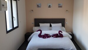 Quarto de hotel com uma cama, duas mesas de cabeceira, uma janela e três quadros na parede.