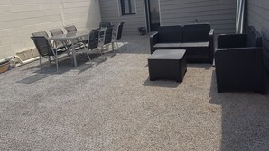 Um pátio externo com mesa, cadeiras, um sofá e um tapete pequeno.
