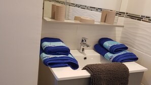 Uma casa de banho moderna com uma pia branca, duas toalhas azuis e uma toalha castanha, com um espelho sobre a pia.