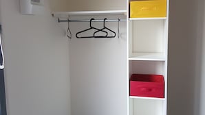 Um armário branco com uma barra de metal para pendurar roupas, uma caixa de armazenamento amarela na prateleira de cima e uma caixa de armazenamento vermelha na prateleira de baixo.