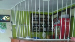 Uma área de recepção com balcão, refrigerador de Coca-Cola e parede verde com placa indicando serviço de alimentação por encomenda.