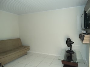 Quarto com sofá bege, mesa de vidro e ventilador de teto.