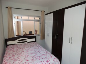 Quarto com cama, guarda-roupa, janela com cortinas e espelho.
