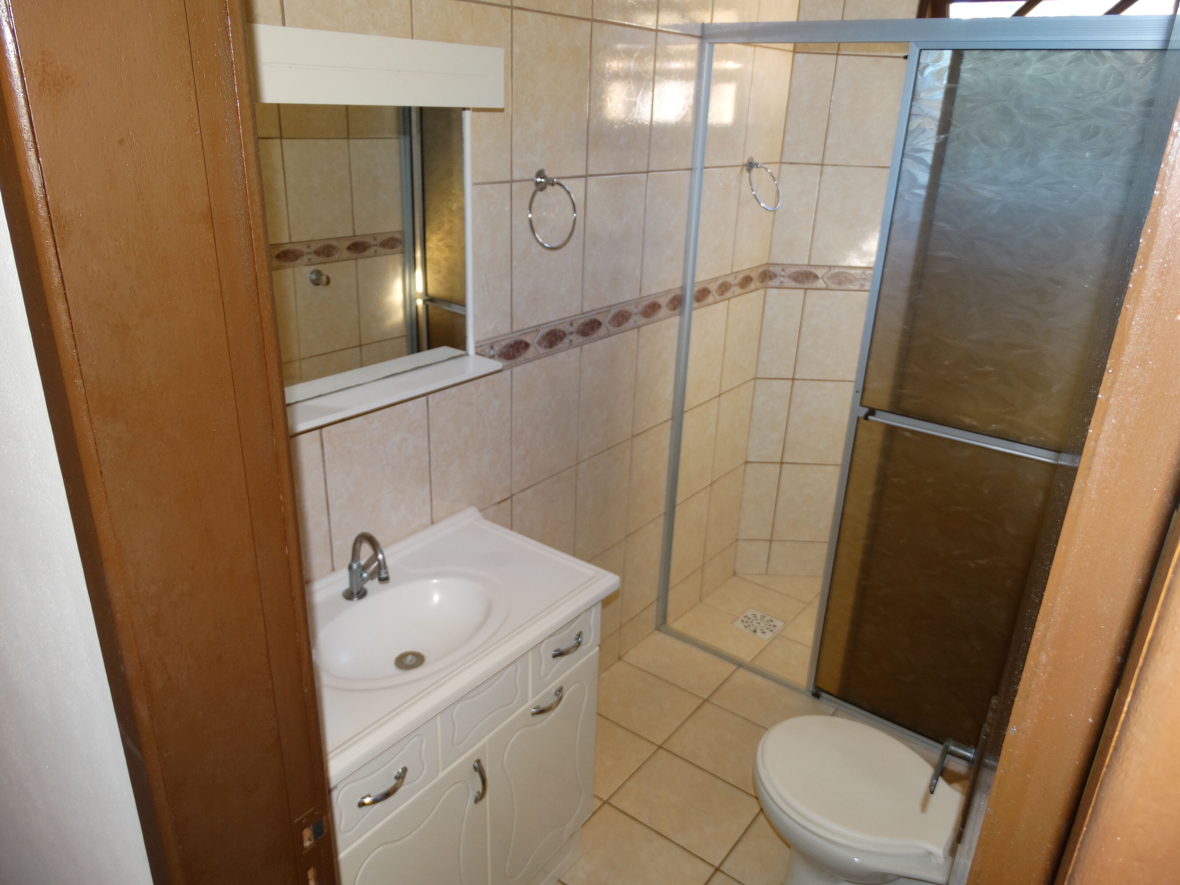 Casa de banho com lavatório, espelho, sanita e zona de duche.