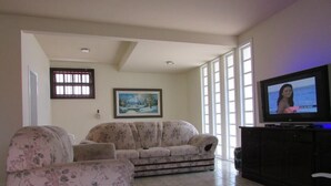 Uma sala de estar com sofá, poltrona, TV e um quadro na parede.