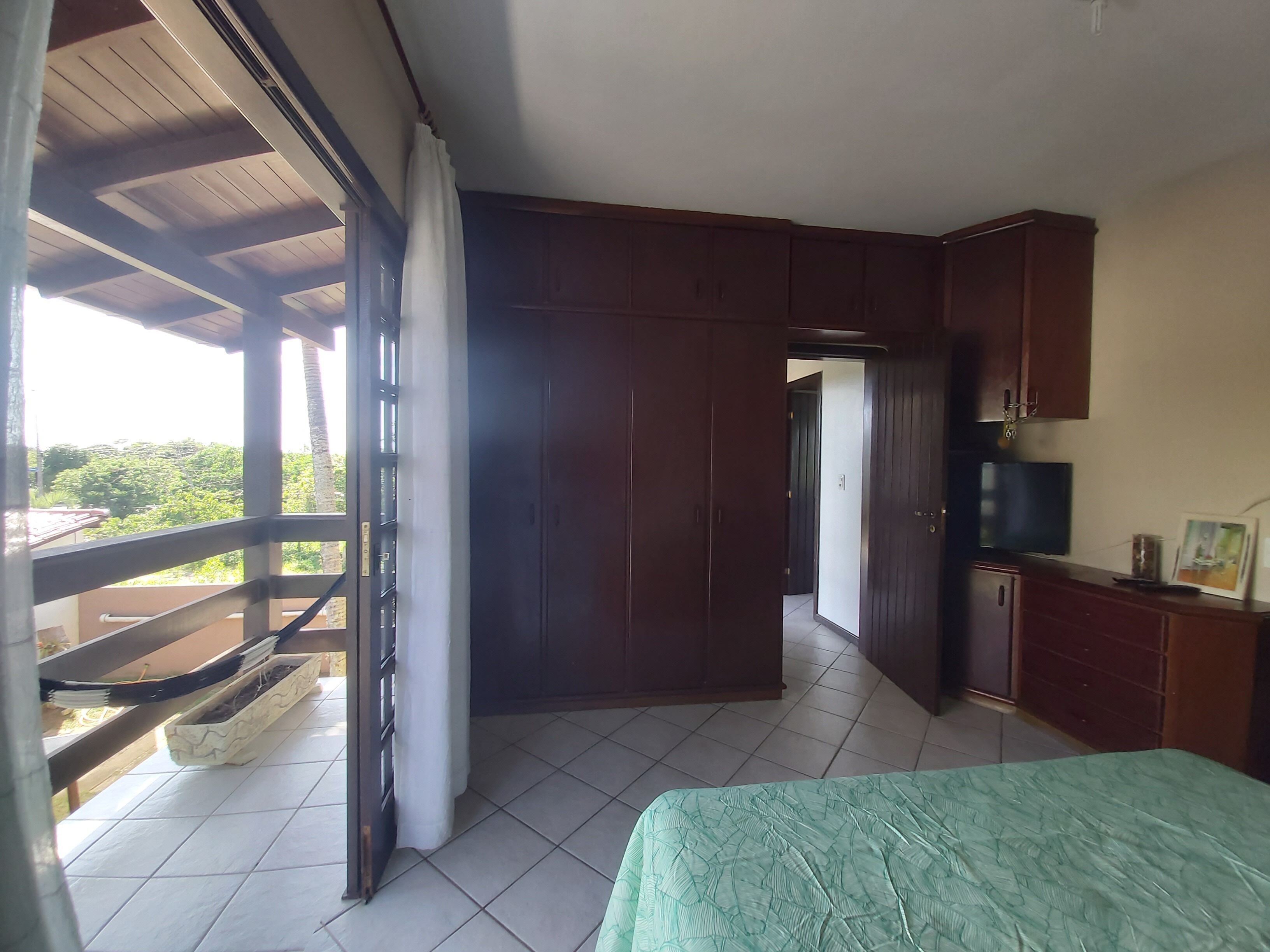 Quarto com cama, televisão e varanda com vista para o verde.