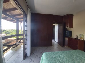 Quarto com cama, televisão e varanda com vista para o verde.