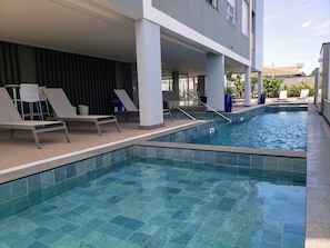 Uma área de piscina moderna ao ar livre, com espreguiçadeiras e água azul cristalina.