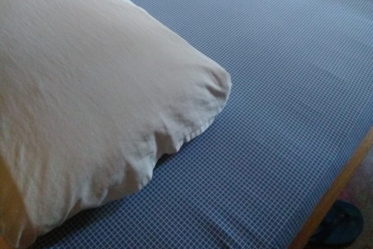 Uma cama de solteiro com colchão azul e travesseiro branco.
