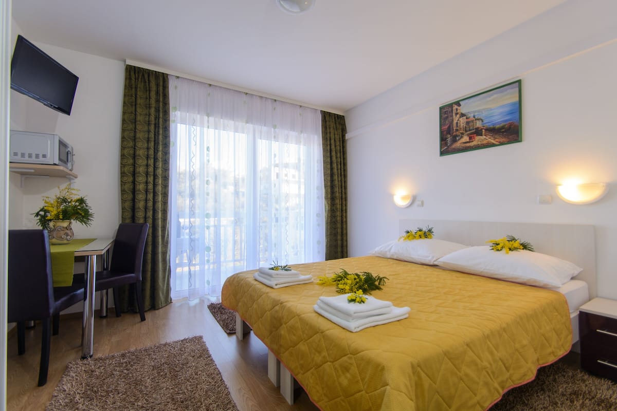 Quarto de hotel com cama, escrivaninha, cadeira, televisão e um quadro na parede.