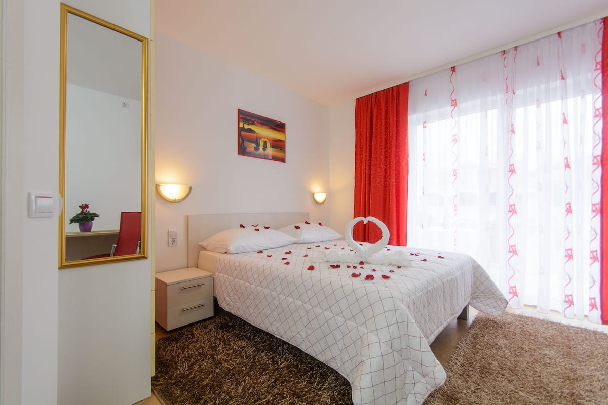 Quarto com cama, mesa de cabeceira, espelho e um quadro na parede.