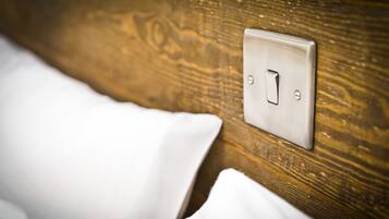 Detalhe de um interruptor de luz numa parede de madeira, um travesseiro branco e um lençol de cama branco.
