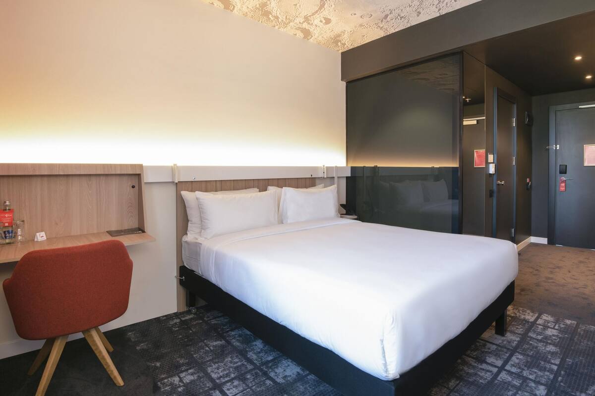 Quarto de hotel com cama, escrivaninha, cadeira e guarda-roupa.