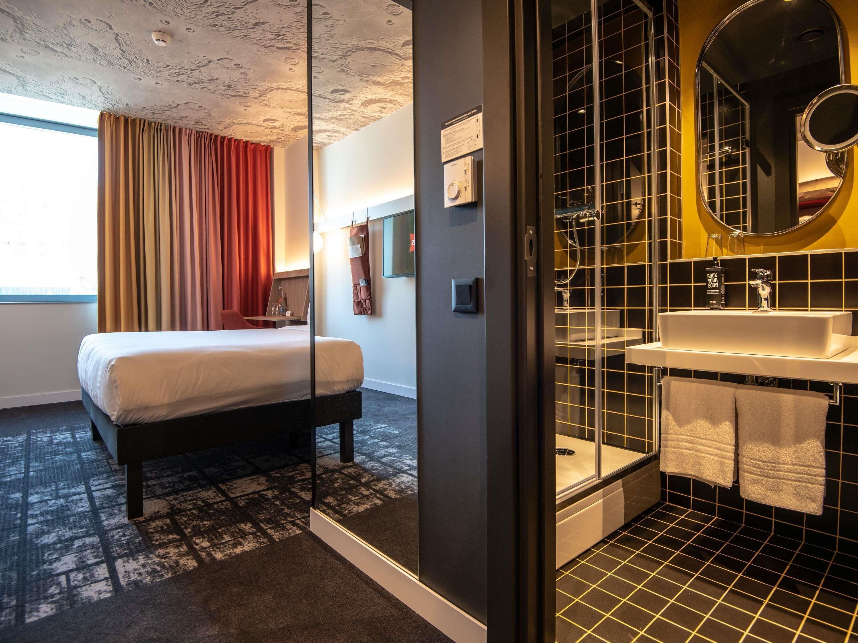 Quarto de hotel com cama, banheiro com pia e espelho, e janela com cortinas.