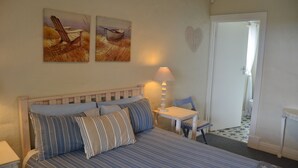 Quarto com cama, mesa de cabeceira com abajur, cadeira e duas pinturas penduradas na parede.
