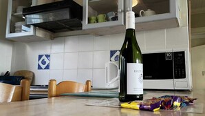 Uma cozinha com micro-ondas, uma garrafa de vinho e um saco de petiscos sobre o balcão.