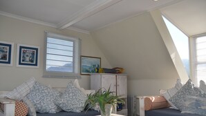 Um quarto aconchegante com um sofá azul, almofadas estampadas, uma mesa de centro branca com uma planta e um armário branco.