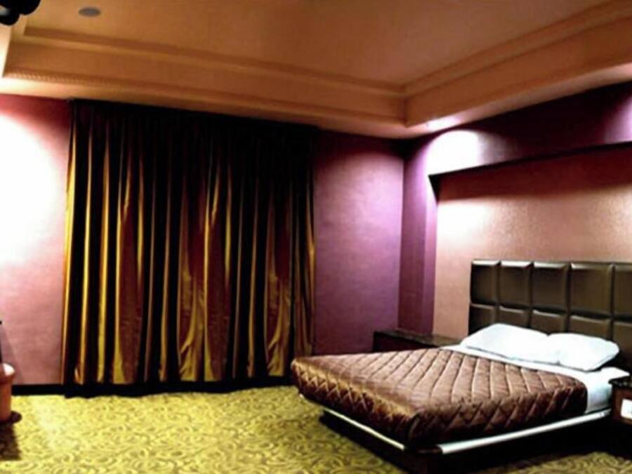 Quarto de hotel com cama, cortinas, mesa de cabeceira e uma pequena planta em vaso.