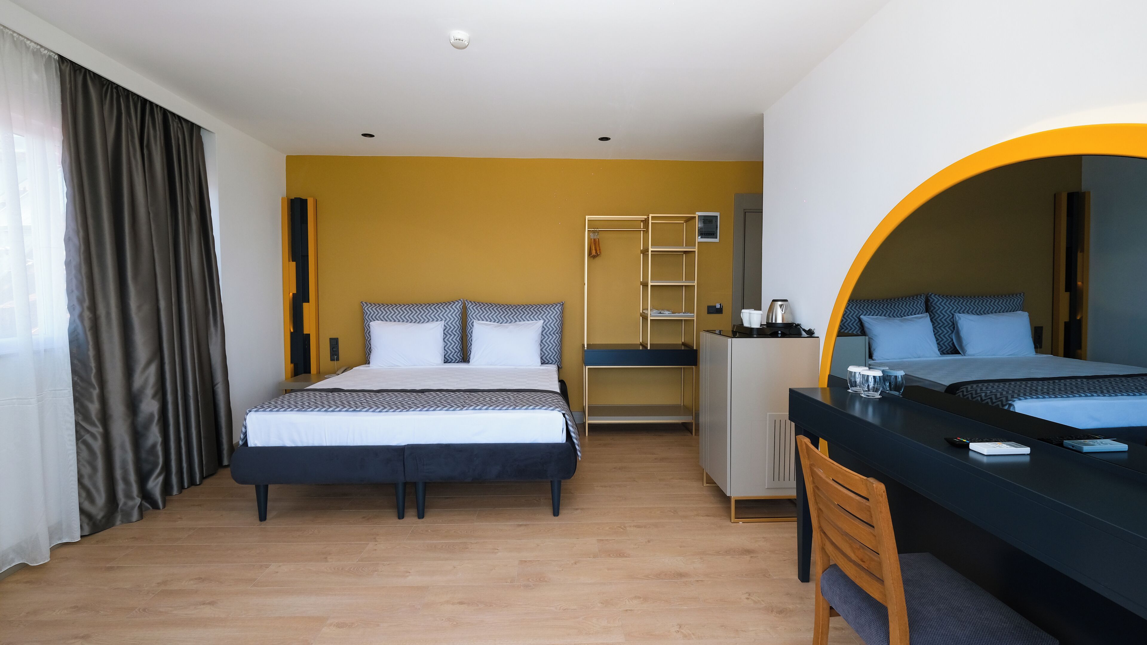 Quarto de hotel com duas camas, uma escrivaninha, uma cadeira, um guarda-roupa e um espelho.