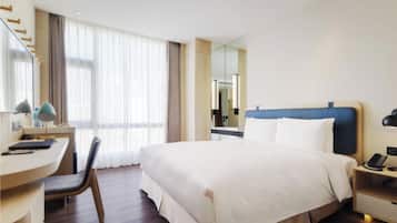 Quarto de hotel com cama, escrivaninha, cadeira e espelho.