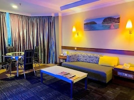 Quarto de hotel com uma mesa redonda, duas cadeiras, um sofá, uma mesinha de centro e um quadro na parede.