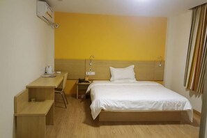 Quarto de hotel com cama, escrivaninha, mesa de cabeceira e luminária na parede.