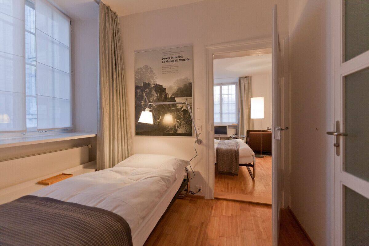 Quarto de hotel com cama, escrivaninha, cadeira e janela.