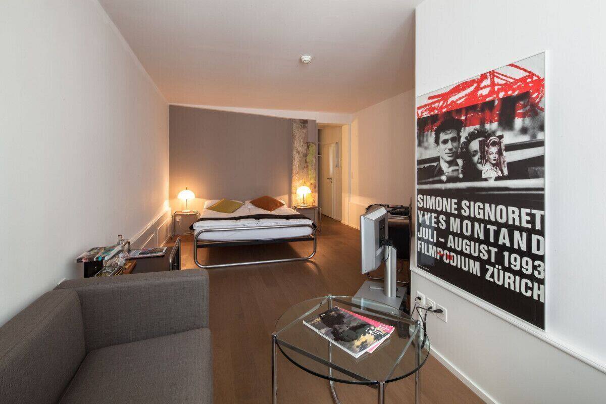 Quarto de hotel moderno com cama, mesa de centro de vidro, televisão e um cartaz na parede.