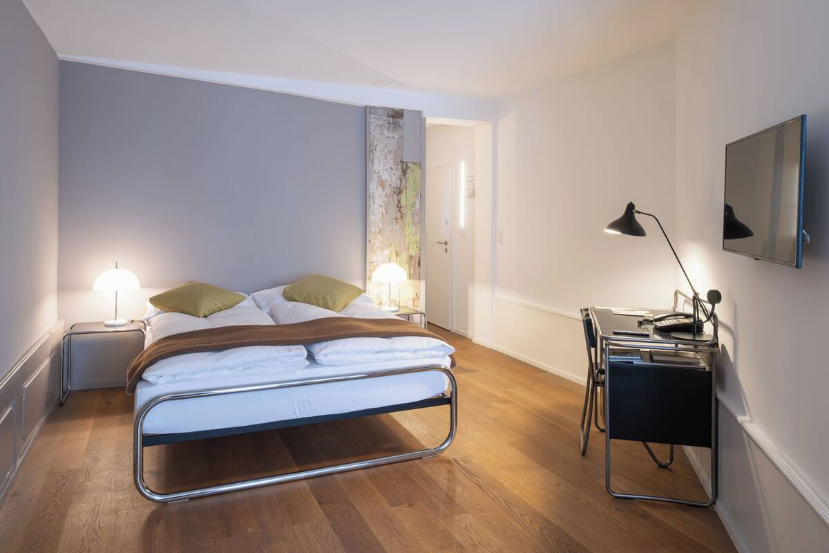 Um quarto com cama, mesas de cabeceira, escrivaninha e uma cadeira.