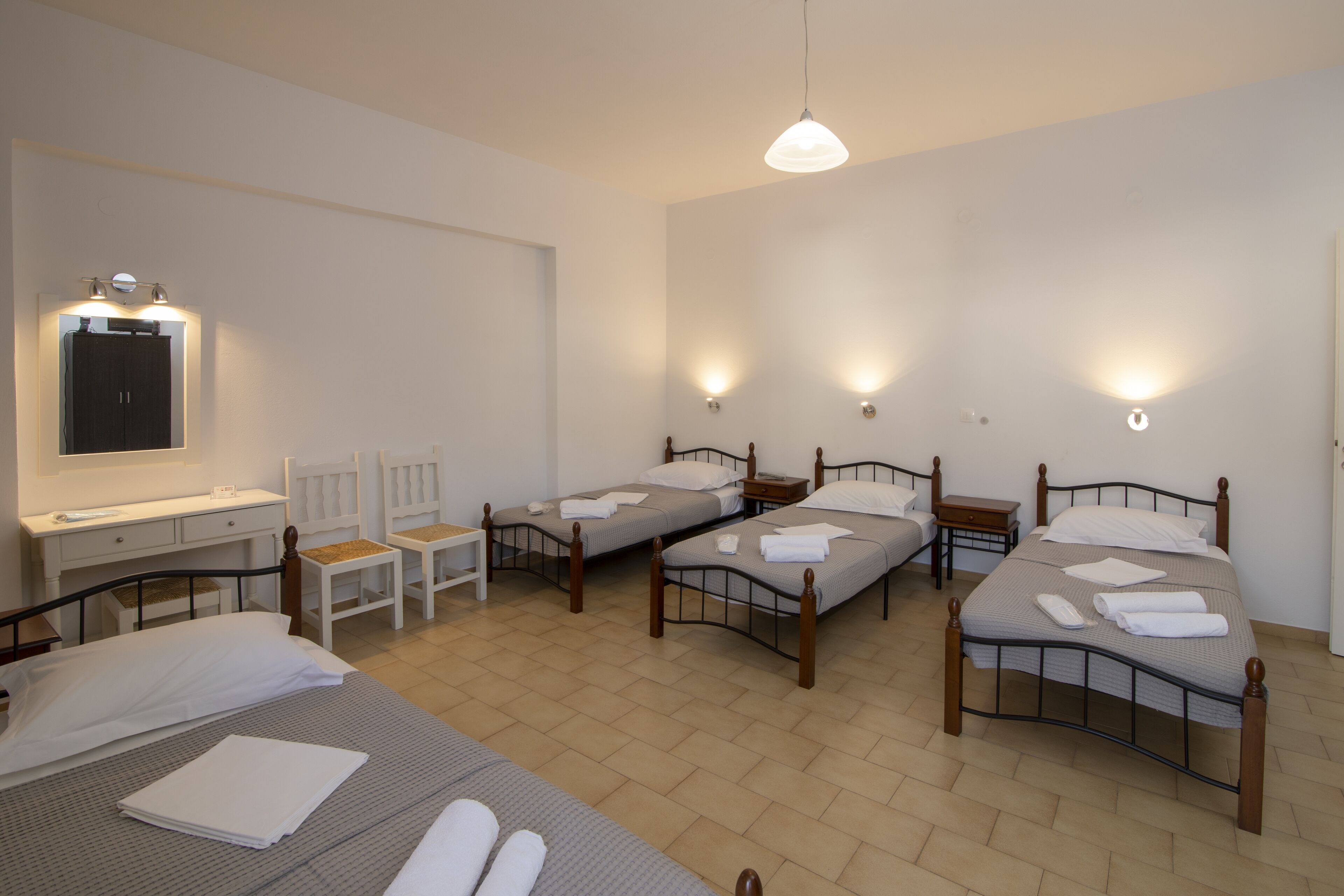 Quarto de hotel com duas camas de solteiro, uma escrivaninha com cadeira, um espelho e luminárias na parede.
