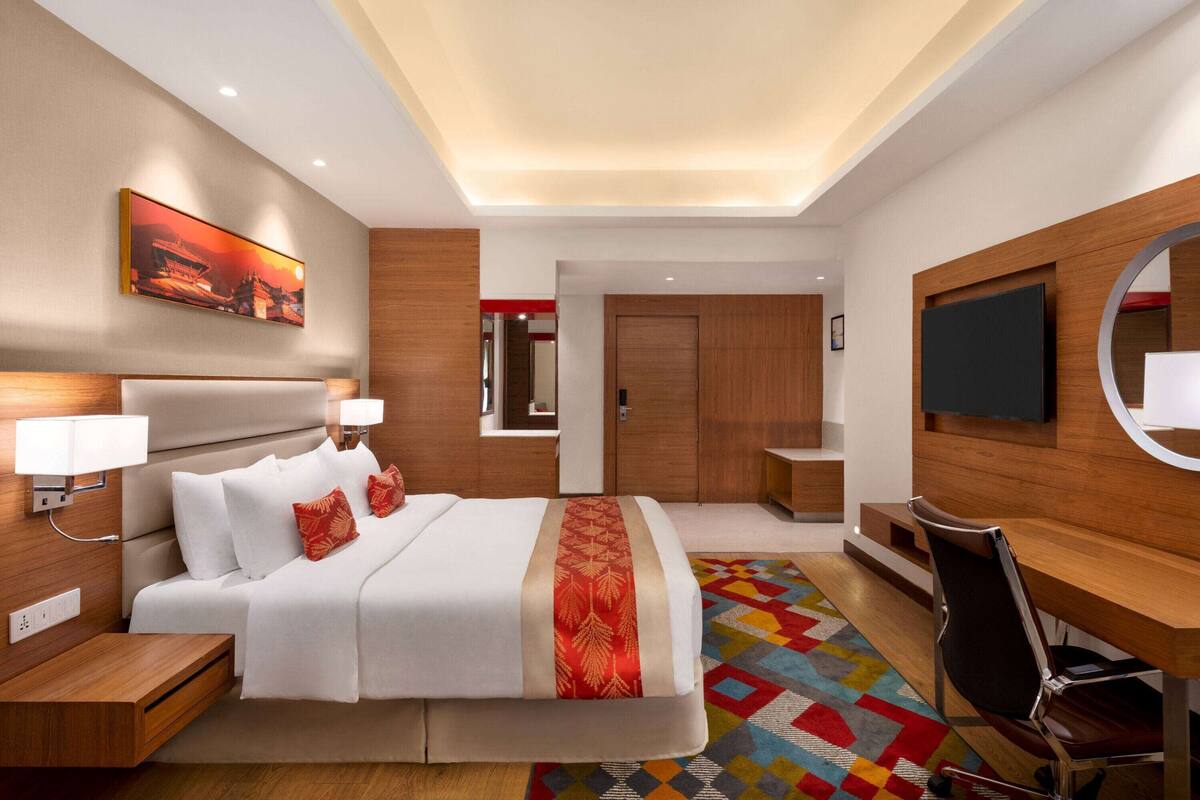 Quarto de hotel moderno com cama, mesas de cabeceira, escrivaninha e espelho.