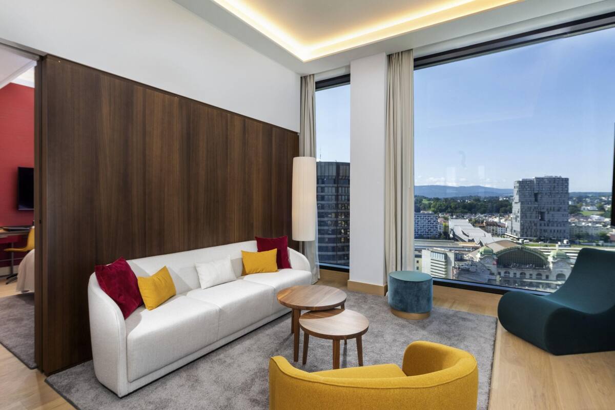 Uma sala de estar moderna com um sofá, uma mesa de centro redonda e vista para um horizonte urbano através de grandes janelas.