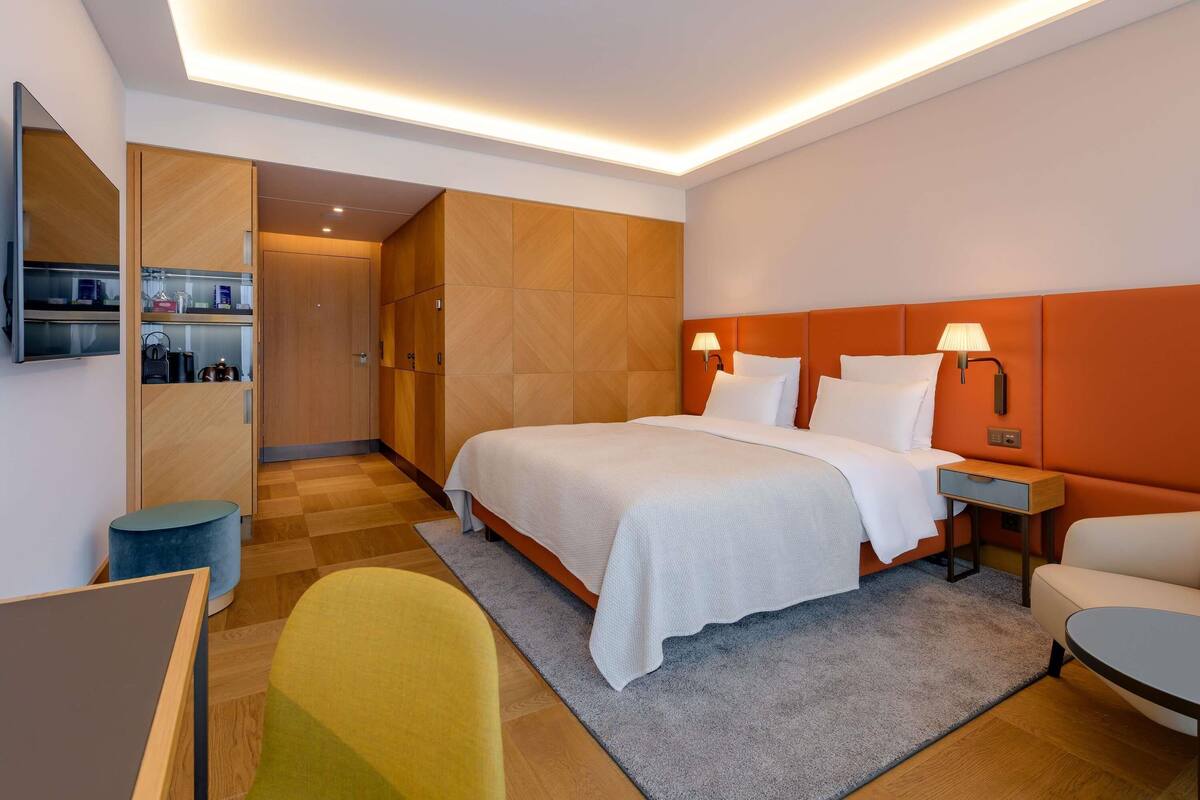 Quarto de hotel moderno com cama, mesas de cabeceira, escrivaninha, cadeira e guarda-roupa.