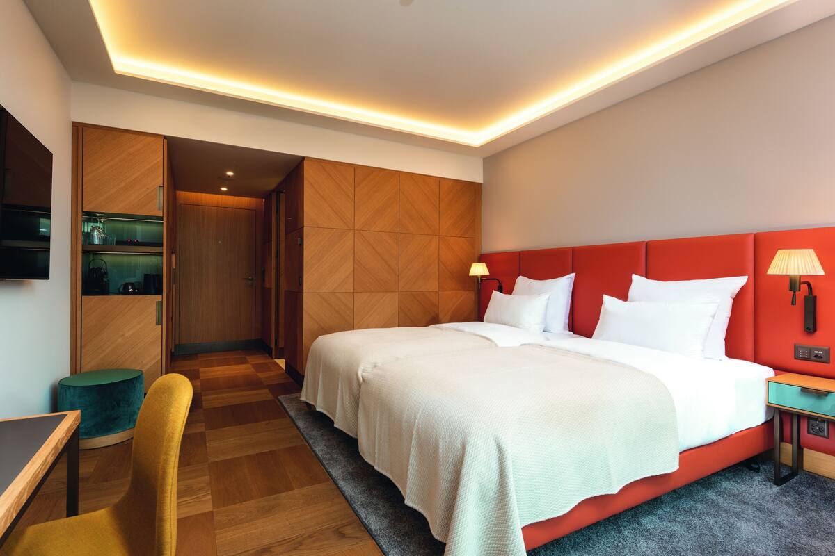 Quarto de hotel moderno com uma cama grande, painel de parede de madeira e uma pequena escrivaninha com cadeira.