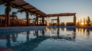 Área da piscina com guarda-sóis, espreguiçadeiras e vista para o pôr do sol.