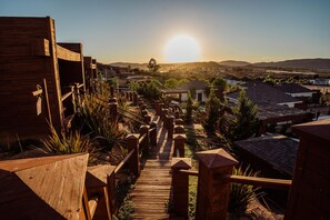 Uma escadaria de madeira leva a uma área residencial com casas e uma vista nítida do pôr do sol ao longe.
