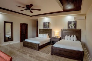 Quarto com duas camas, cabeceiras de madeira, um ventilador de teto e um espelho.