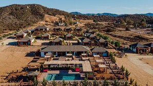 Um resort com várias acomodações semelhantes a bangalôs, uma área de piscina central e um cenário montanhoso ao fundo.