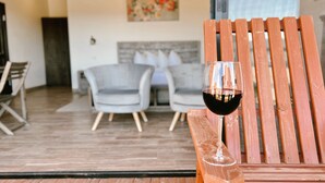Uma cadeira de madeira, um copo de vinho tinto, um poltrona cinza e um sofá moderno em um ambiente bem iluminado com piso de madeira.