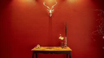 Pared vermelha com cabeça de veado fixada, mesa de madeira com um vaso e flores, e um pequeno objeto decorativo.