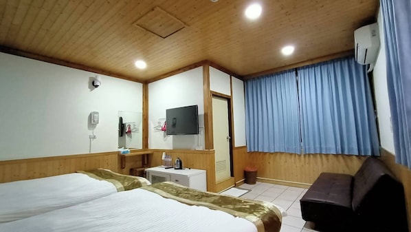 Quarto de hotel com cama, escrivaninha, espelho, televisão e janela com cortinas.