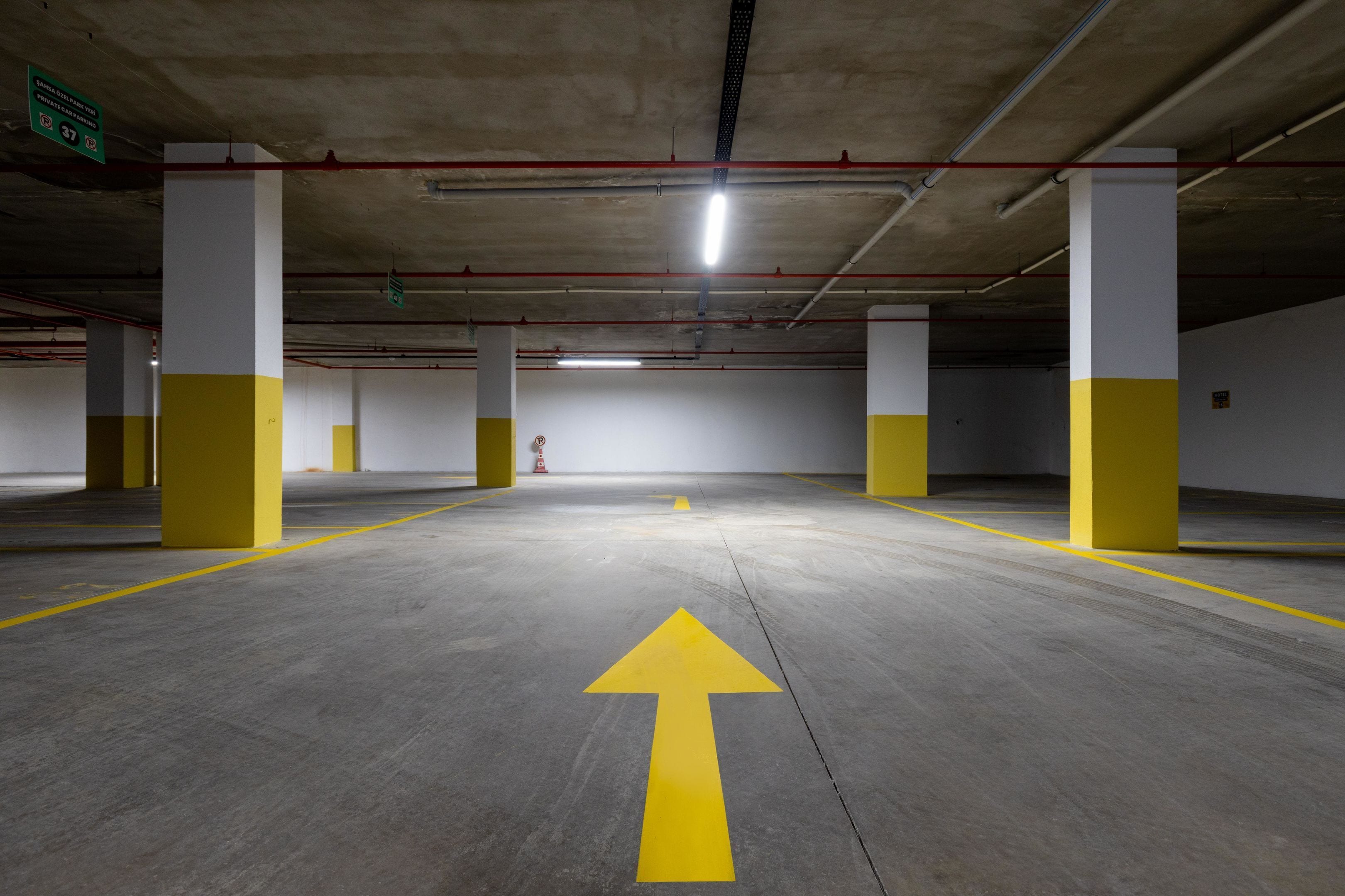 Garagem subterrânea com pilares amarelos e setas indicativas no chão.