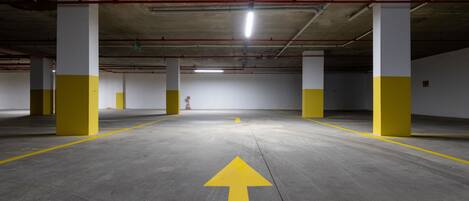 Garagem subterrânea com pilares amarelos e setas indicativas no chão.