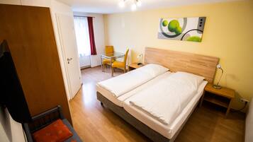 Quarto de hotel com cama de casal, escrivaninha, cadeira e uma pequena mesa.